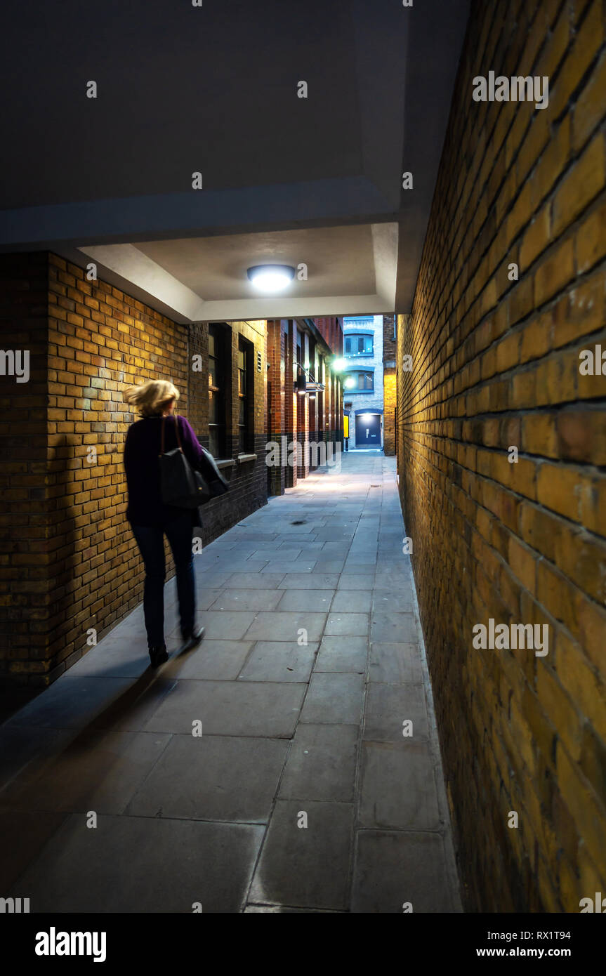 Rear view of a young woman walking in a Semi dark paved passageway ...