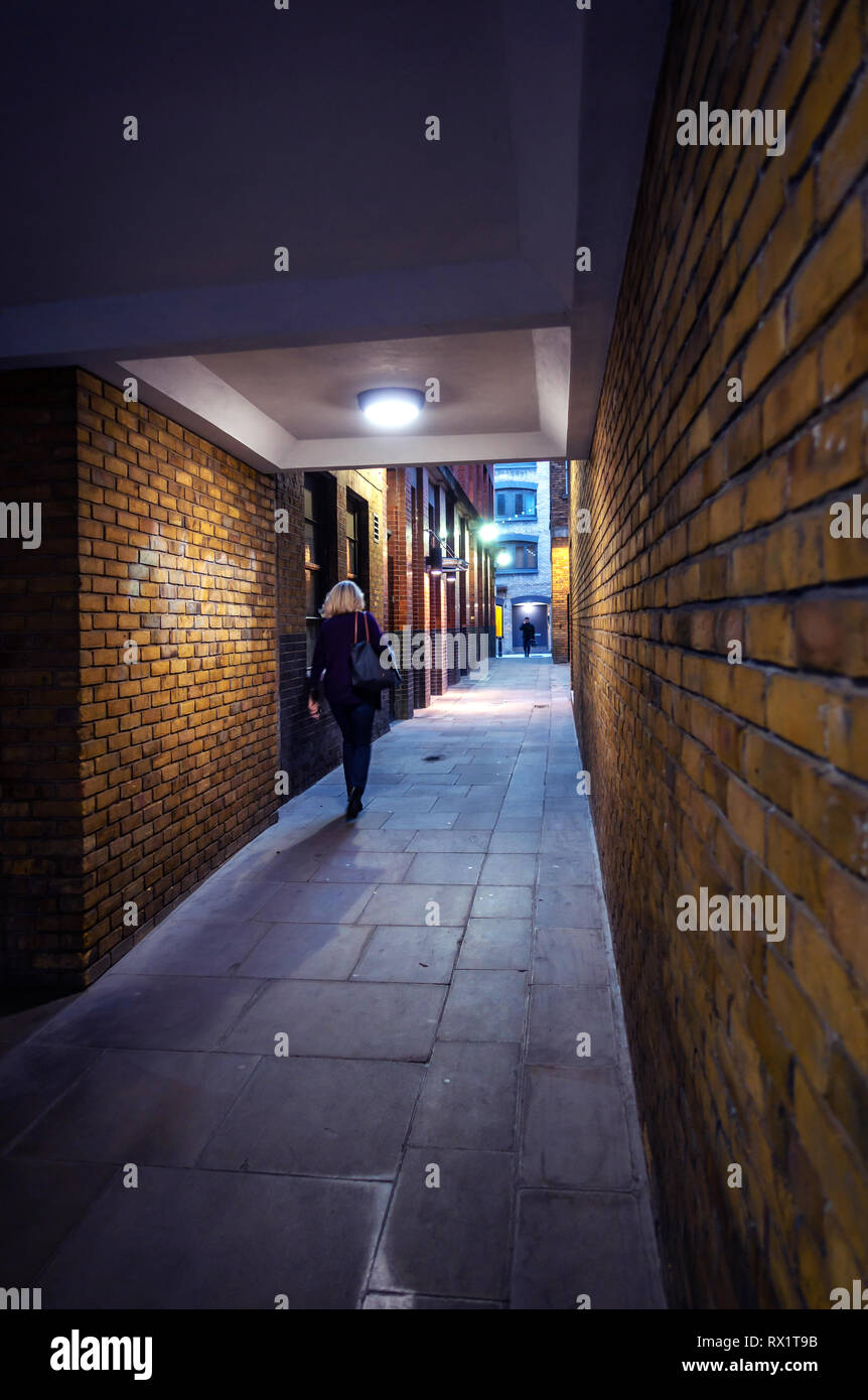 Rear view of a young woman walking in a Semi dark paved passageway ...