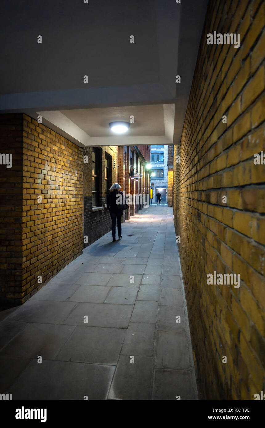 Rear view of a young woman walking in a Semi dark paved passageway ...