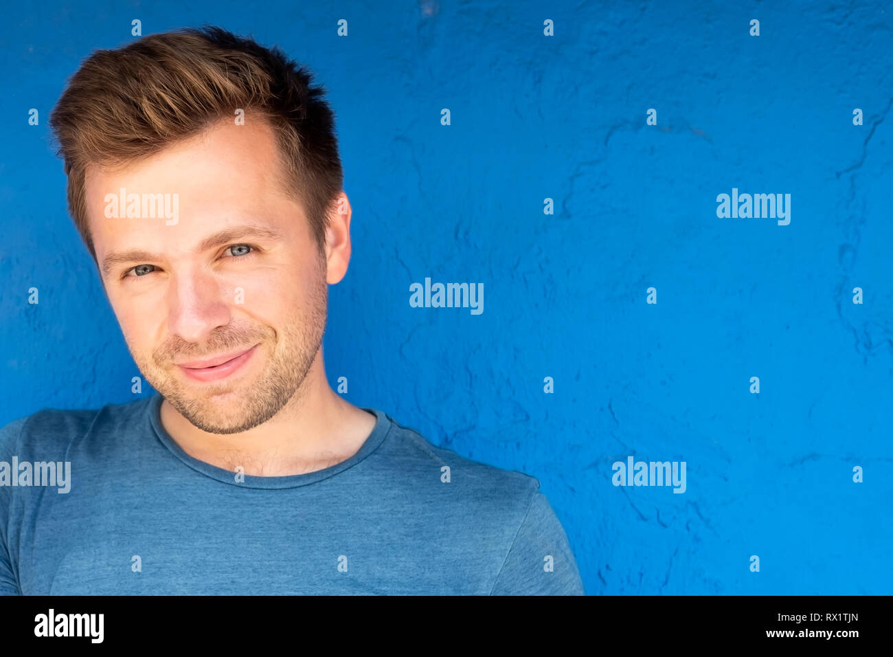 Handsome sunburnt man smiling against blue background and looking at ...