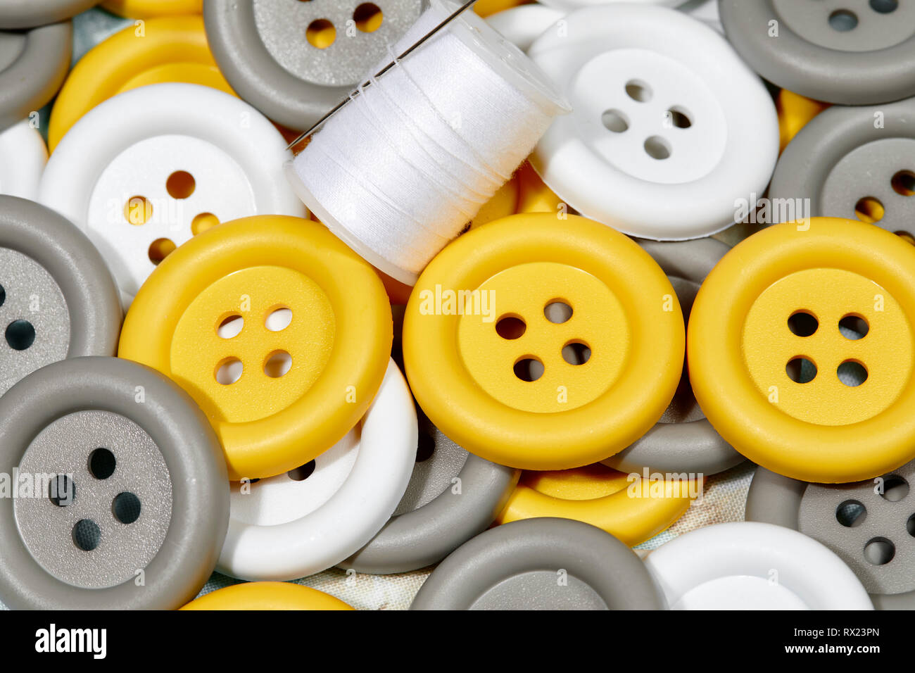 Close up of large yellow, gray and white buttons and spool of thread ...