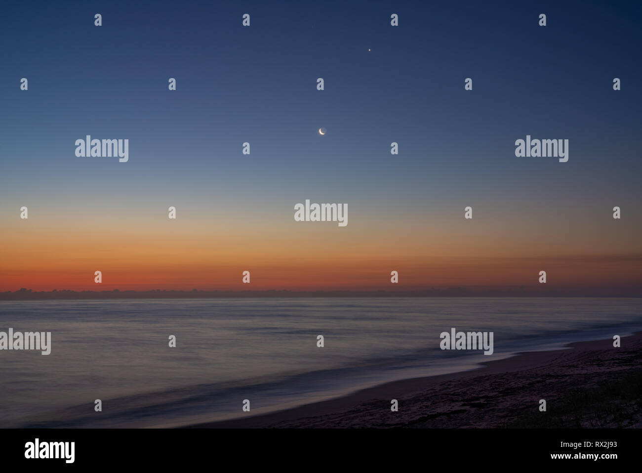 The crescent moon rises above the ocean shortly before sunrise in ...