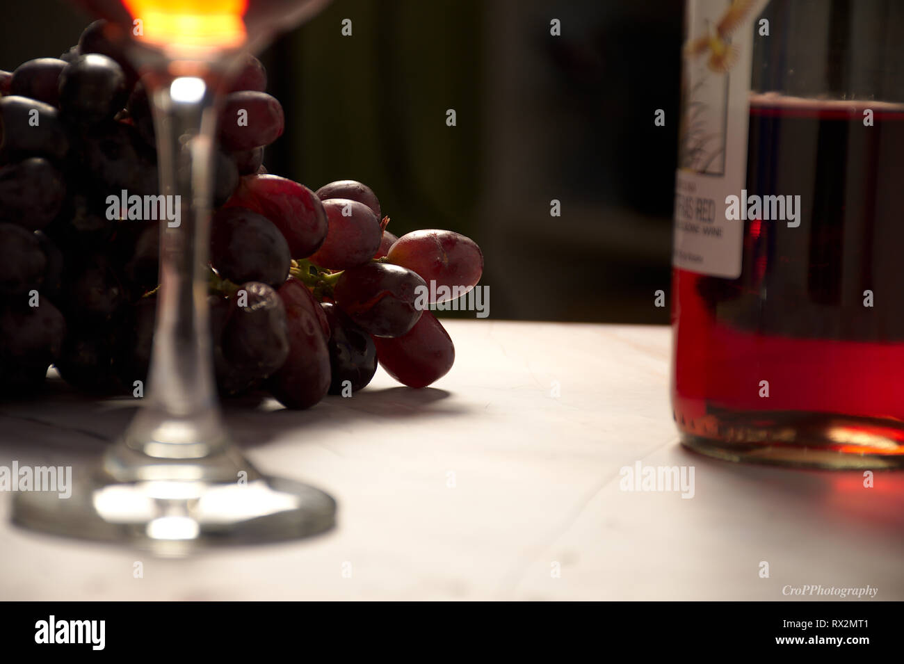 Glass of red wine with bottle and red grapes back light Stock Photo - Alamy