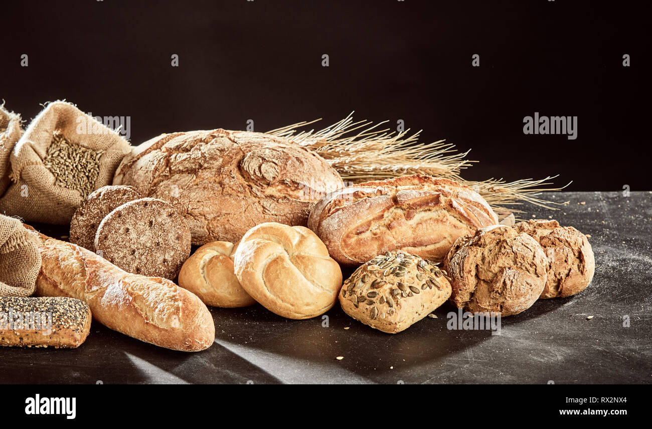 Fresh bread loaves assortment piled on dark table surface with grains ...