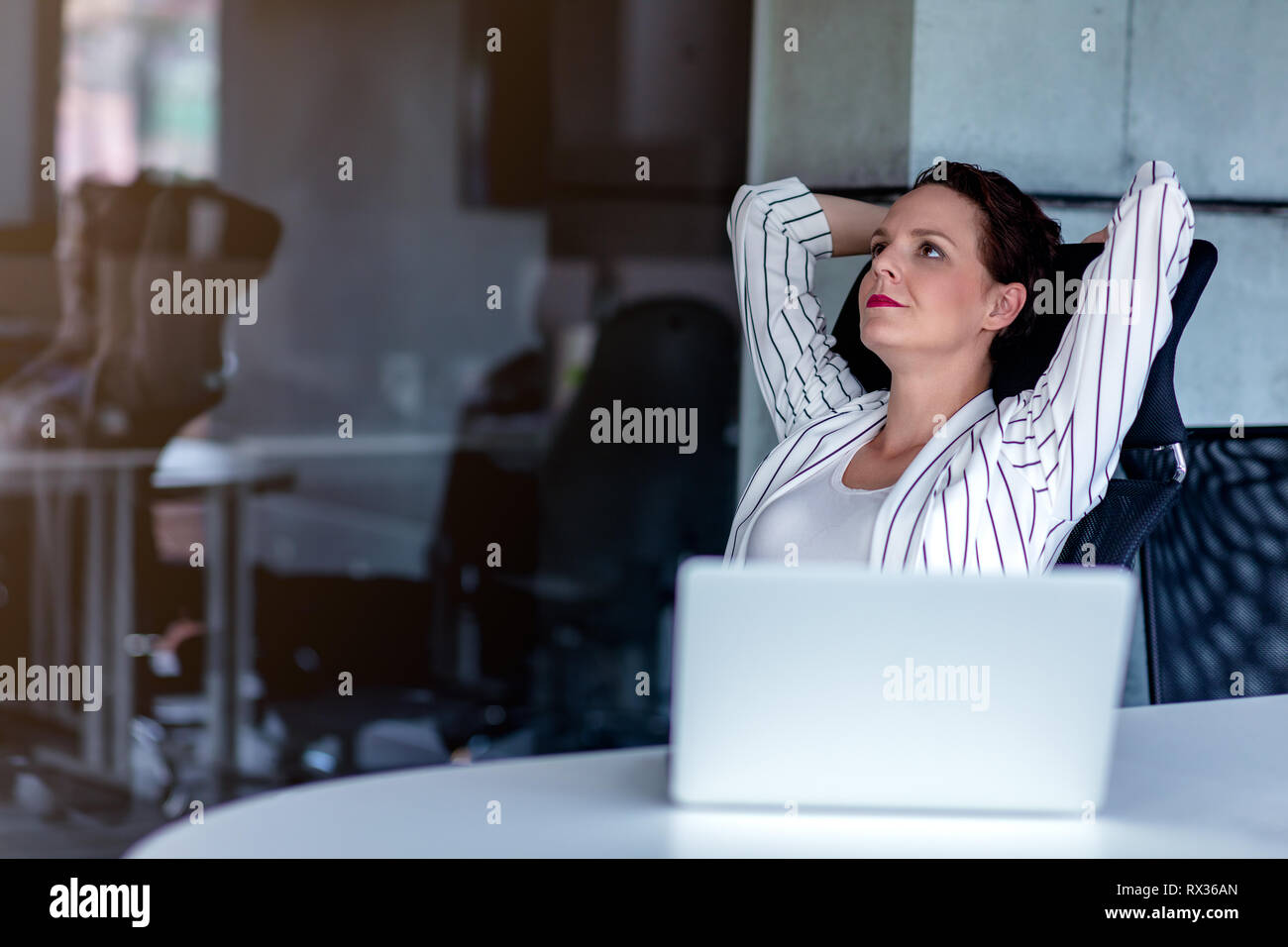 Relaxing at working place. Attractive young woman holding hands behind ...