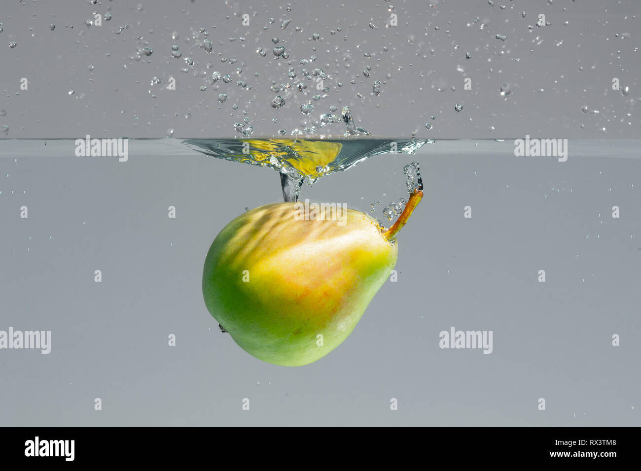 Green pear falls into water and creates beautiful air bubbles and water ...
