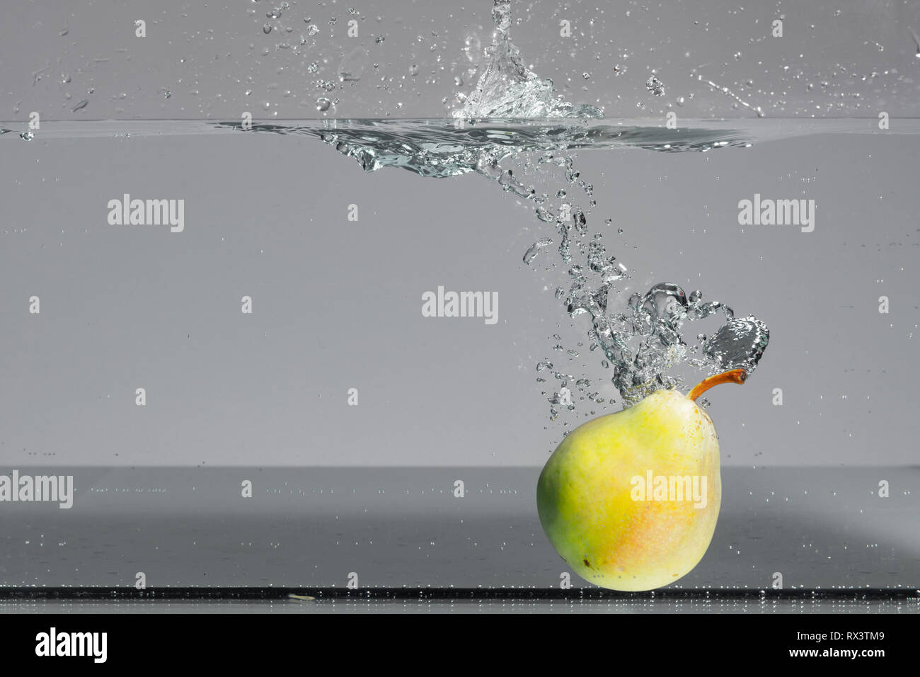 Green pear falls into water and creates beautiful air bubbles and water ...
