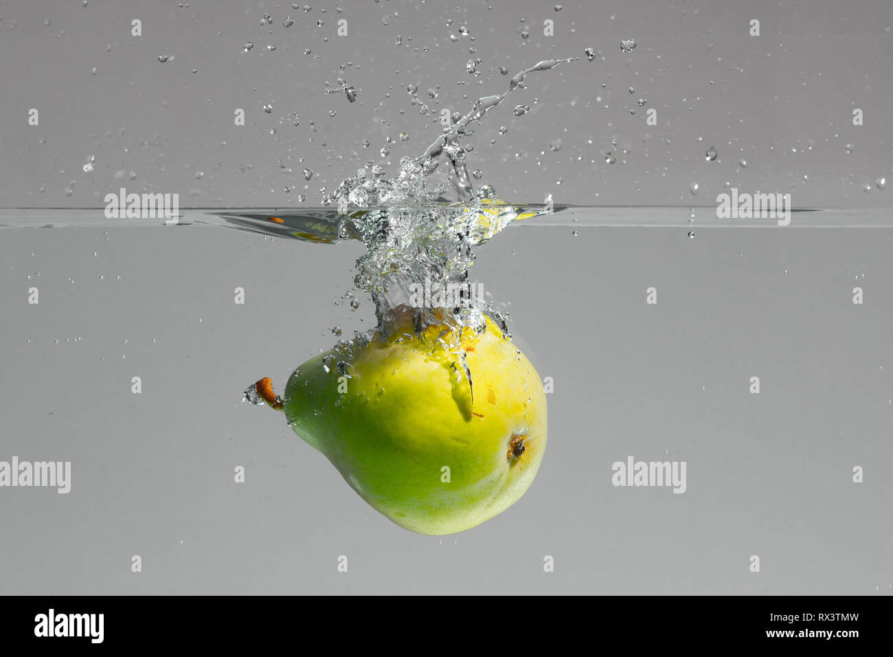 Green pear falls into water and creates beautiful air bubbles and water ...