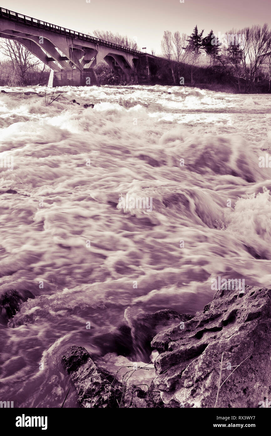 Rushing waters of a swollen river during the rainy season with a bridge ...