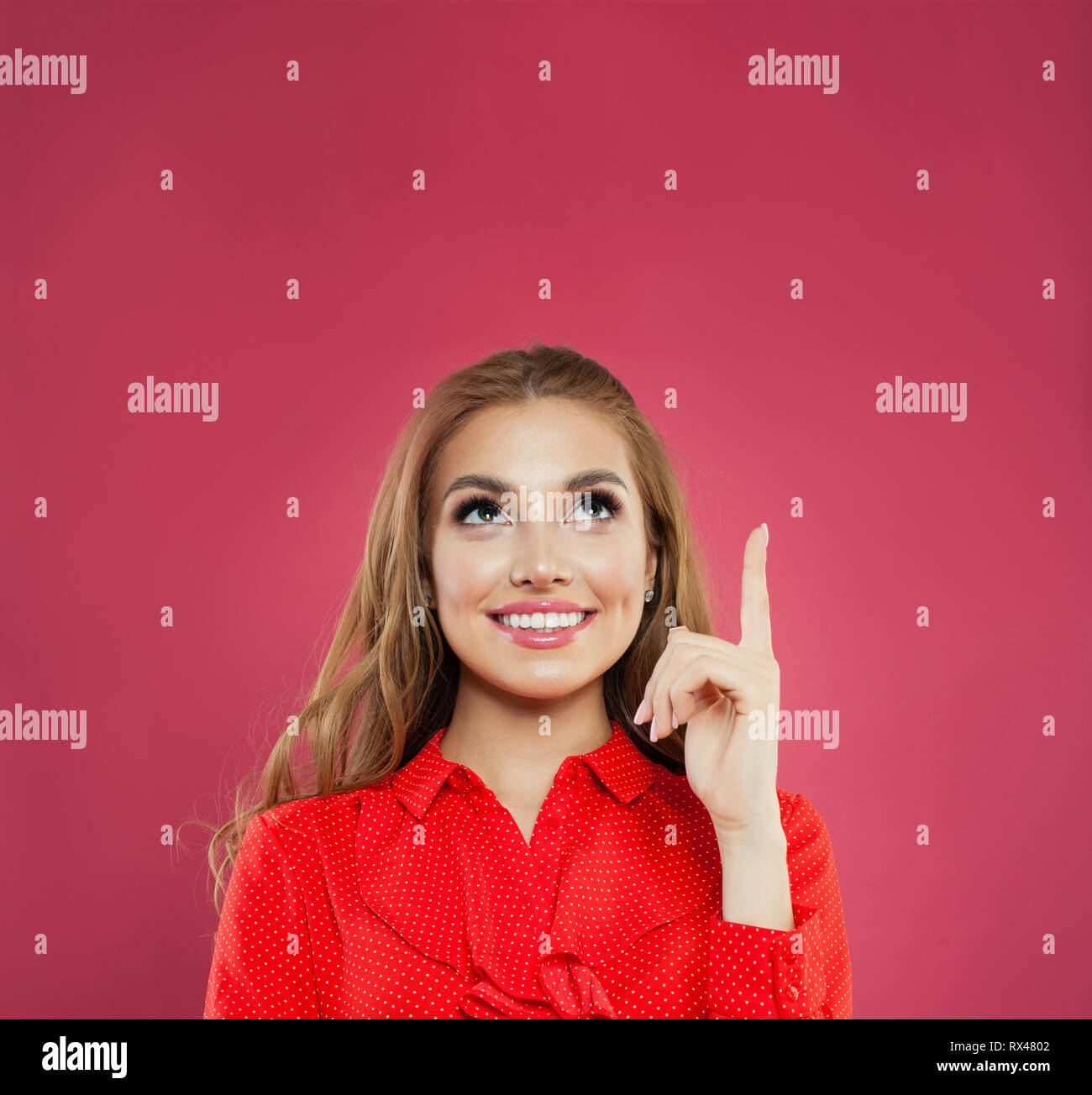 Happy woman pointing up her finger and smiling on bright colorful pink ...