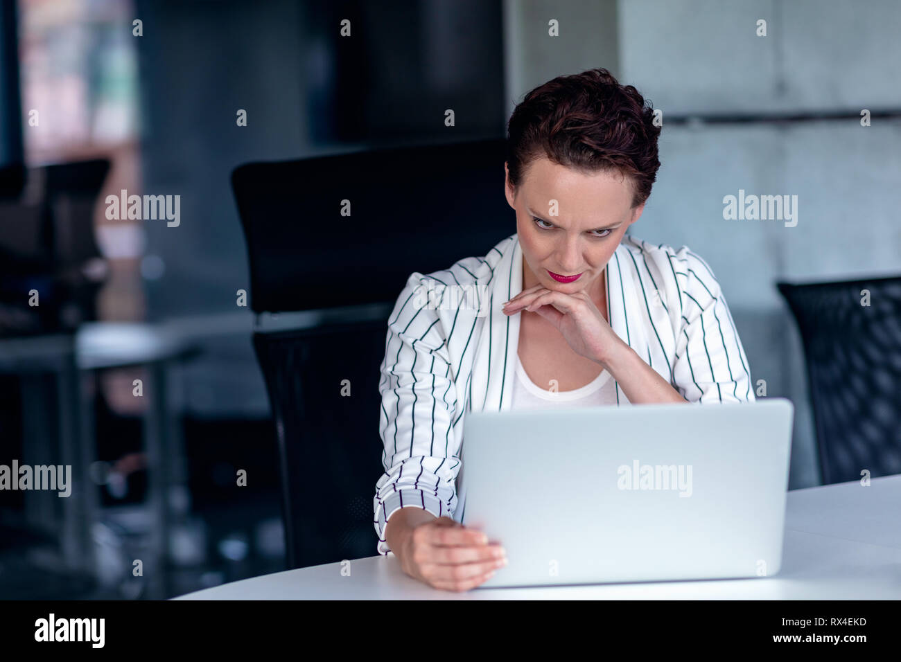 A young businesswoman sits behind her laptop computer frowning with her ...