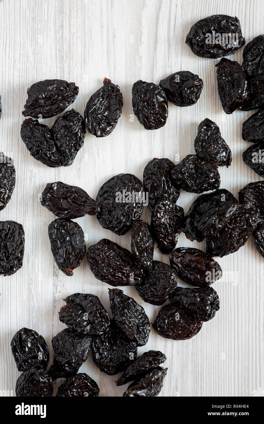 Dry prunes on a white wooden surface, top view. Flat lay, from above ...
