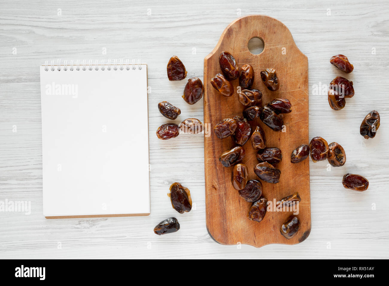 Dried dates on rustic wooden board, blank notepad over white wooden ...
