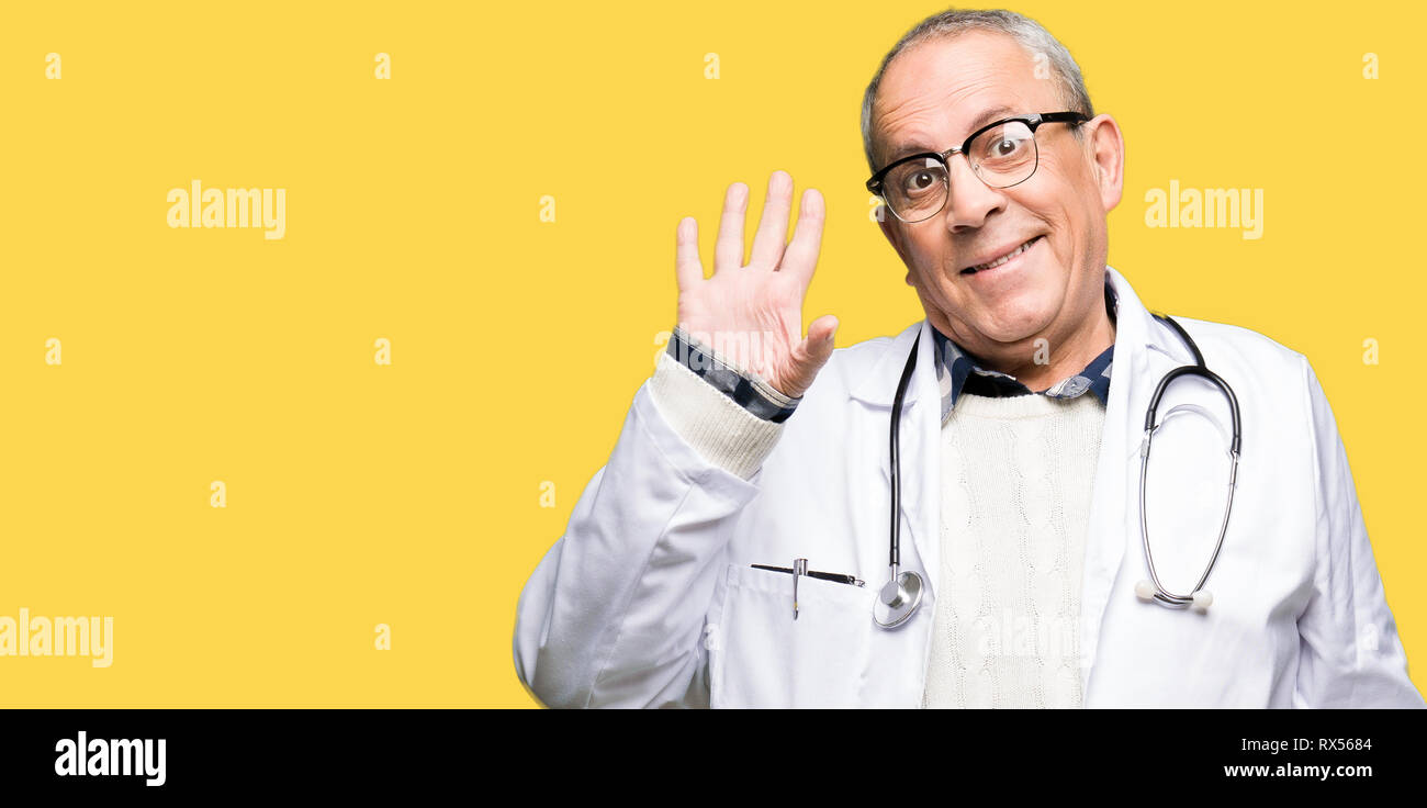 Handsome senior doctor man wearing medical coat Waiving saying hello ...