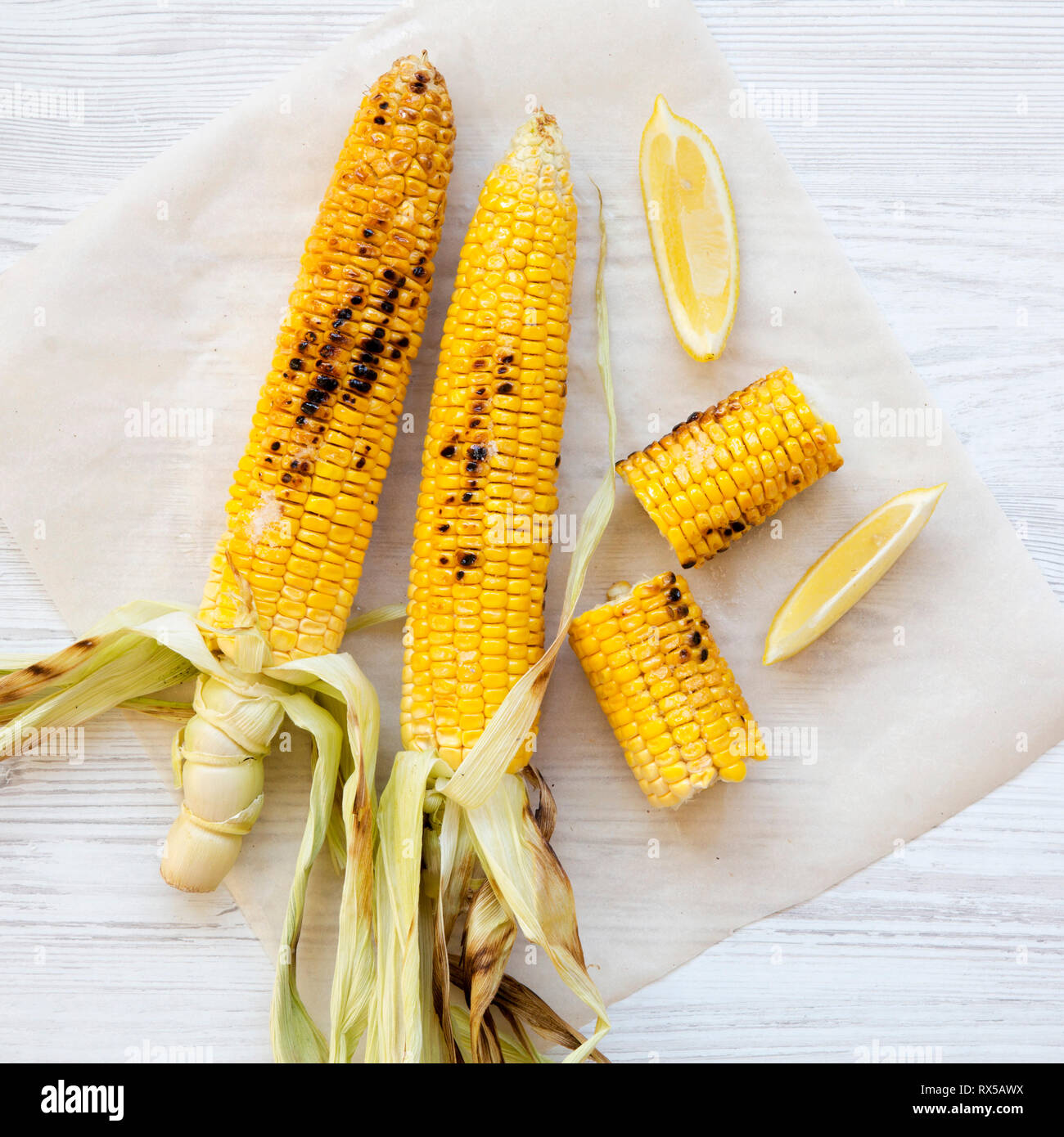 Grilled corn on the cob with slices of lemon over white wooden ...