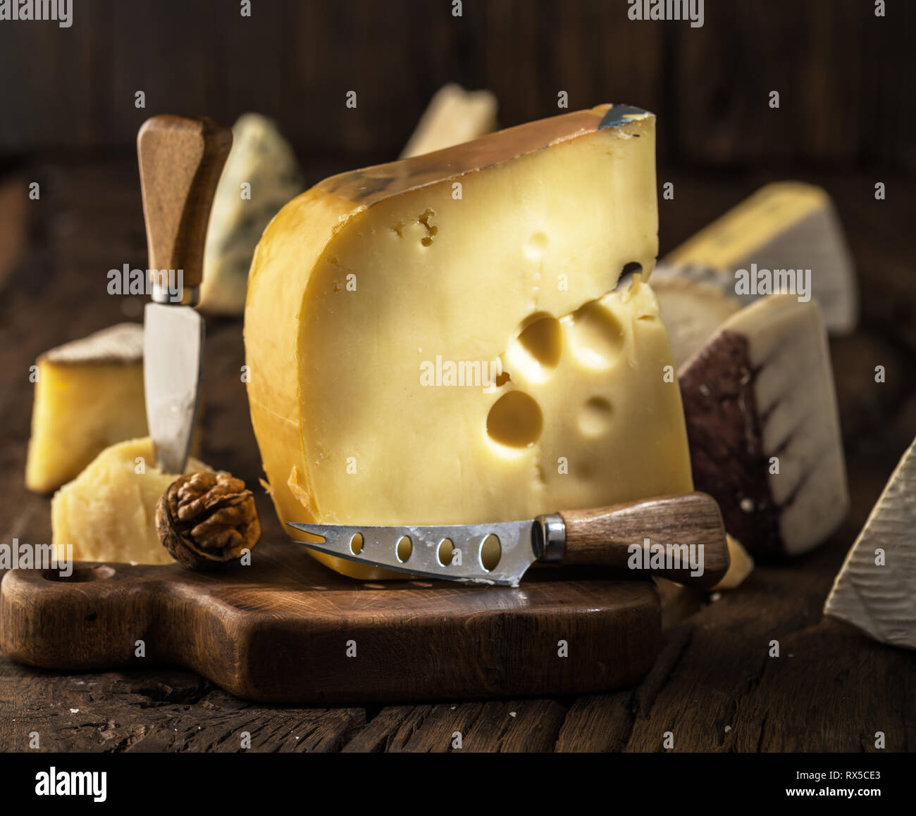 Piece of cow's milk Maasdam cheese on wooden board. Range of cheeses at ...
