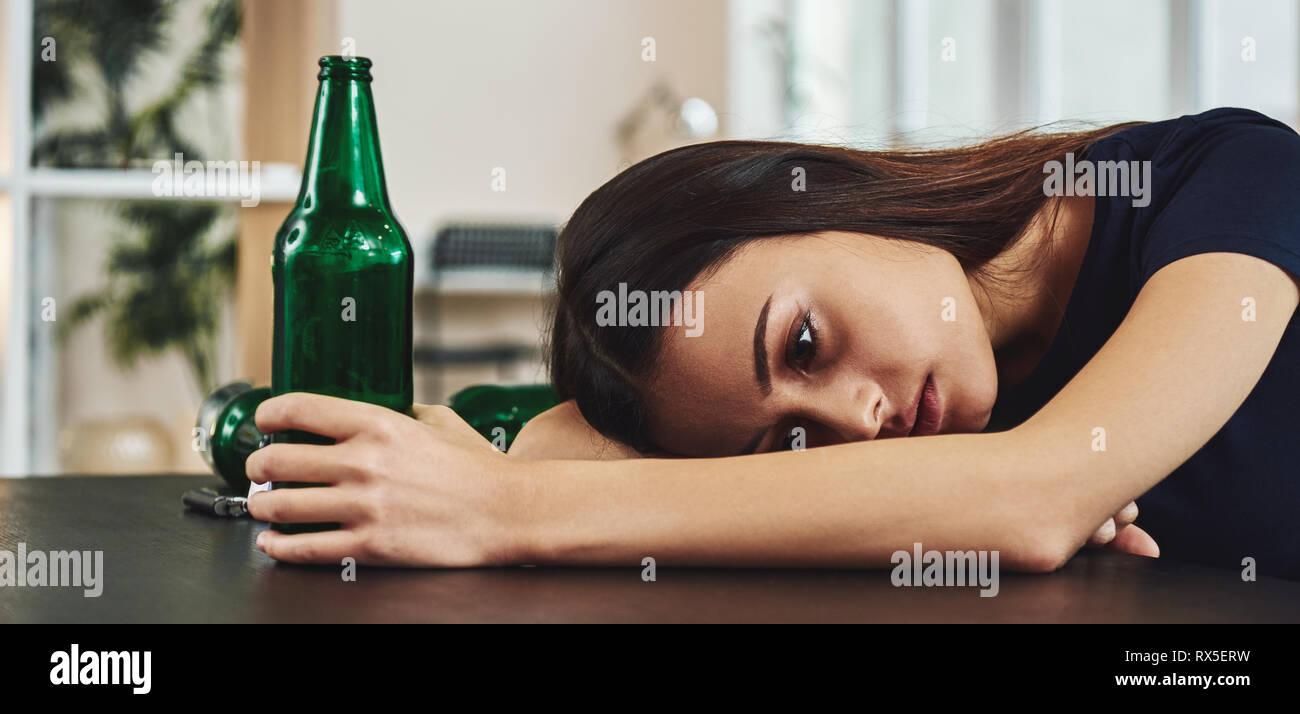 Dark-haired, sad and wasted alcoholic woman lying on a table, in the ...