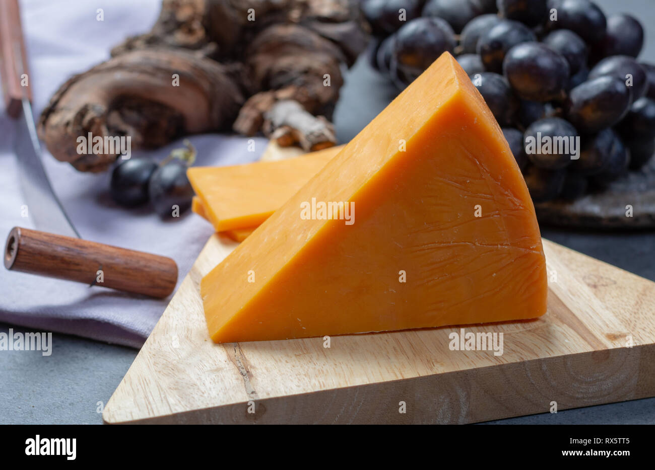 Piece of hard orange Cheddar cheese served with black grape, close up ...