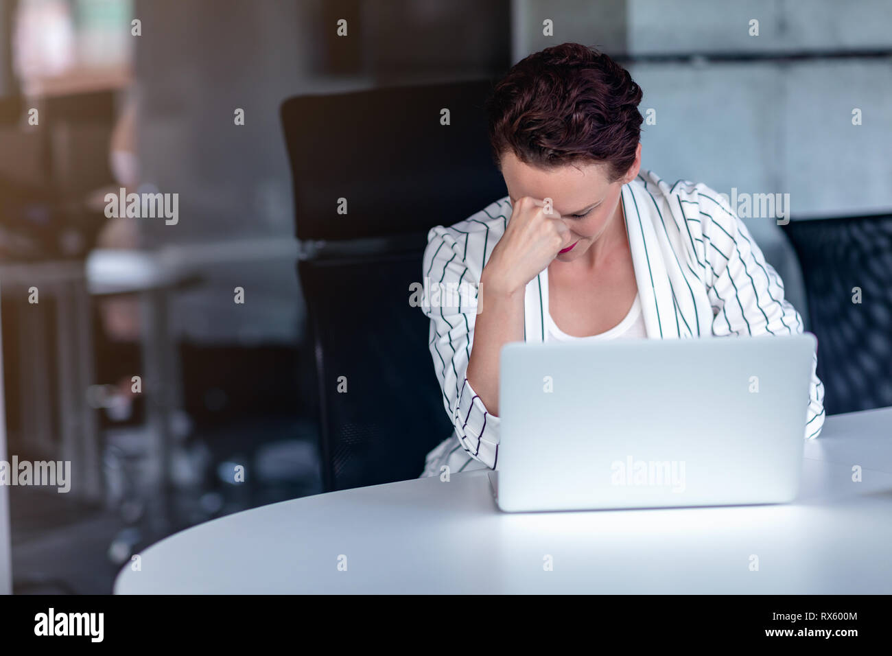 A young businesswoman sits behind her laptop computer frowning with her ...