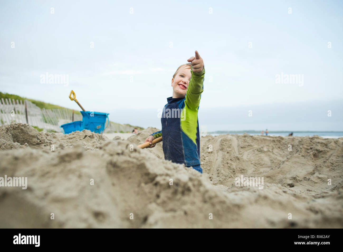 Side view of playful boy pointing away while digging sand at beach ...
