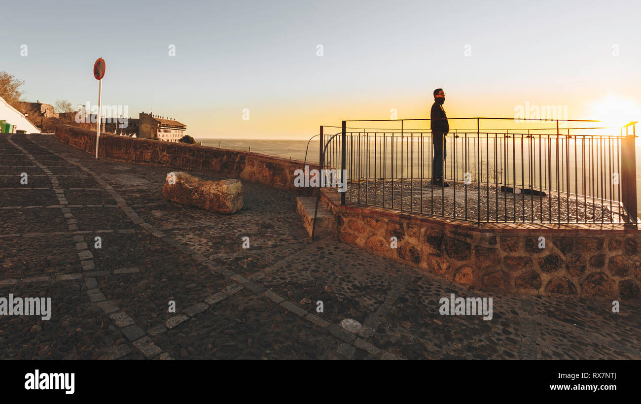 A young man is standing on the lookout looking at the dawn with sun in ...