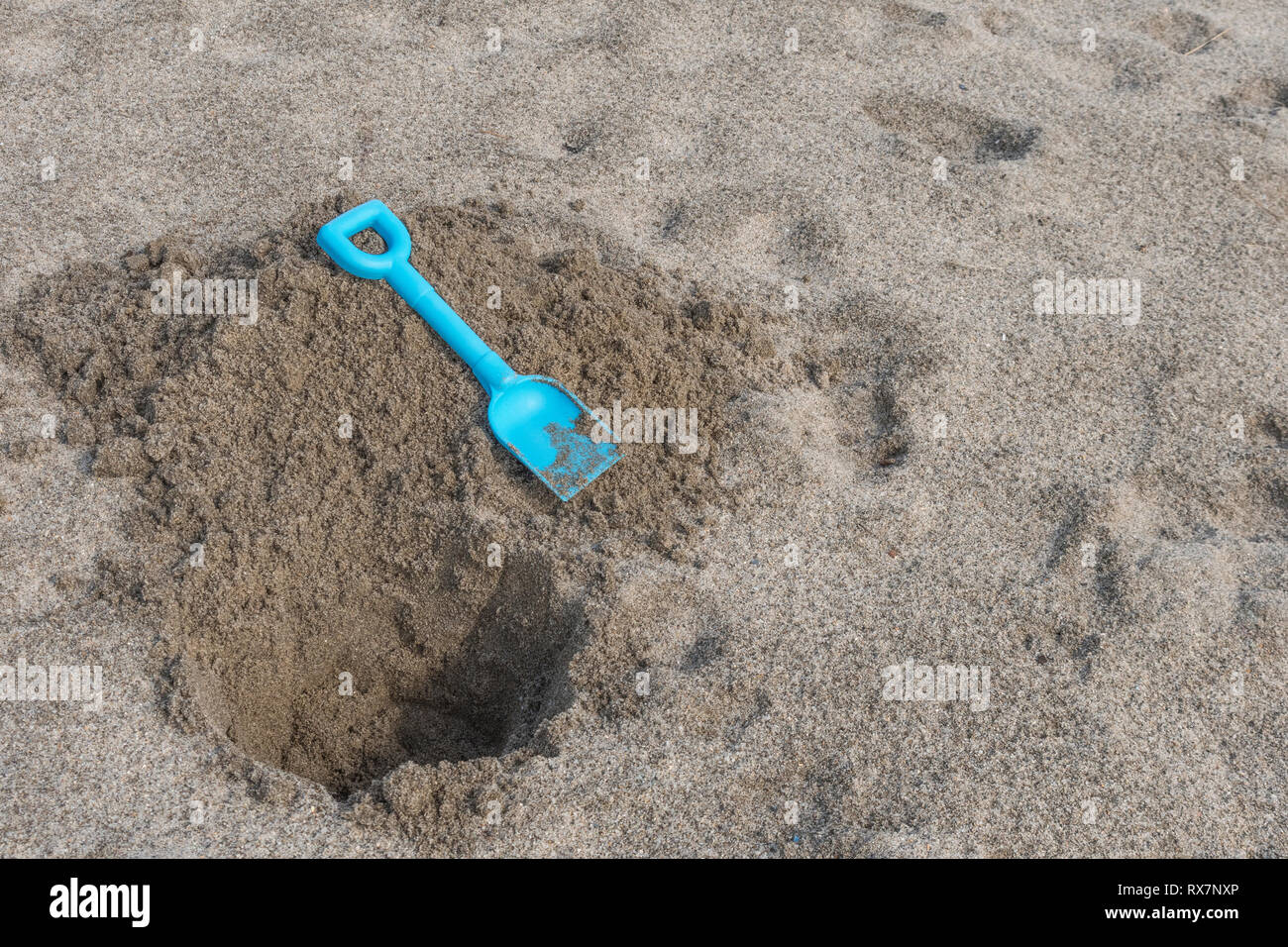 Seaside hole dug into sand, with kids blue spade. Metaphor 'dig a hole ...