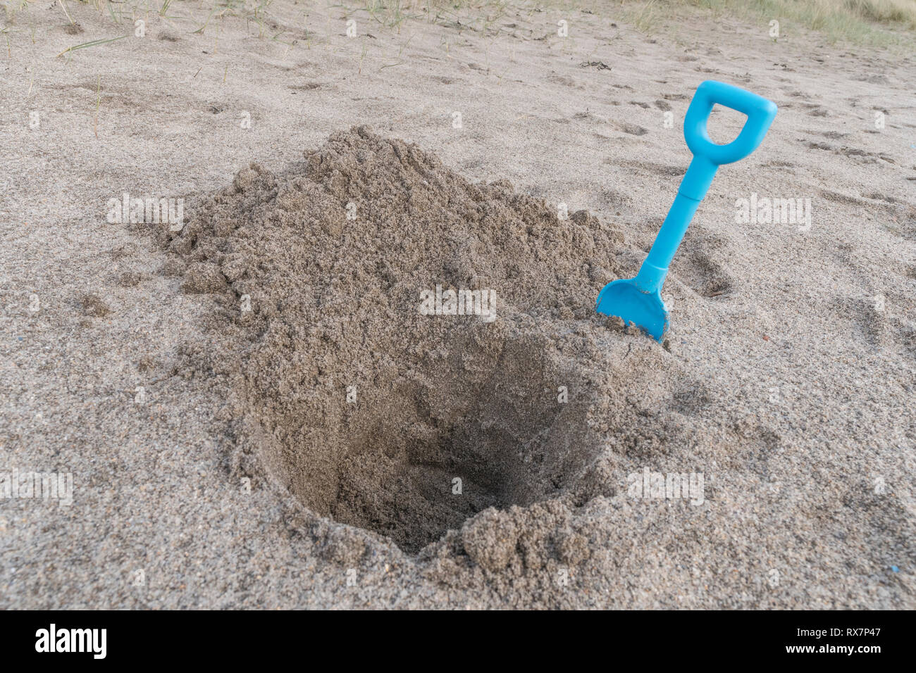 Seaside hole dug into sand, with kids blue spade. Metaphor 'dig a hole ...