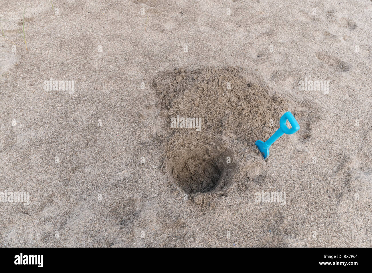 Seaside hole dug into sand, with kids blue spade. Metaphor 'dig a hole ...