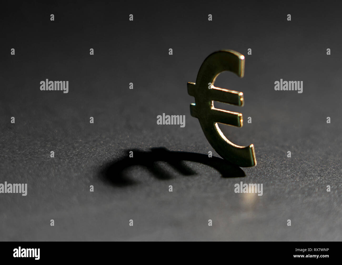 Gold Euro sign on a black background illuminated by the spotlight and ...