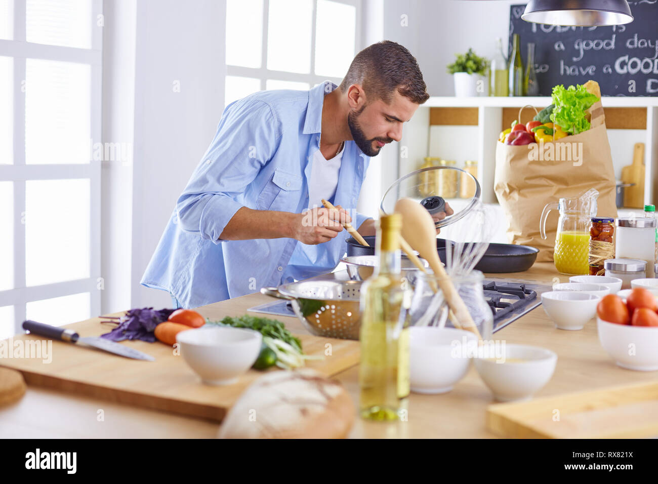 Smiling and confident chef standing in a large kitchen tasting a cooked ...