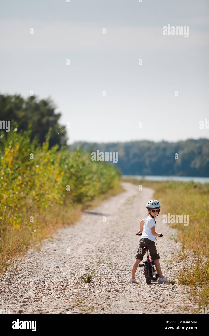 Small child with helmet learning ride a bicycle on park off road. Turns ...