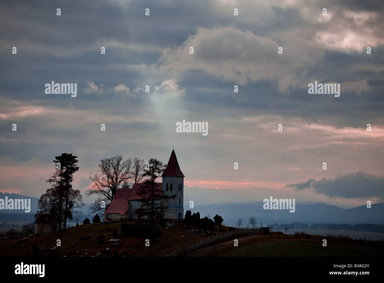 Dramatic sunset time, church on the horizon. Rays of the sun going thru ...