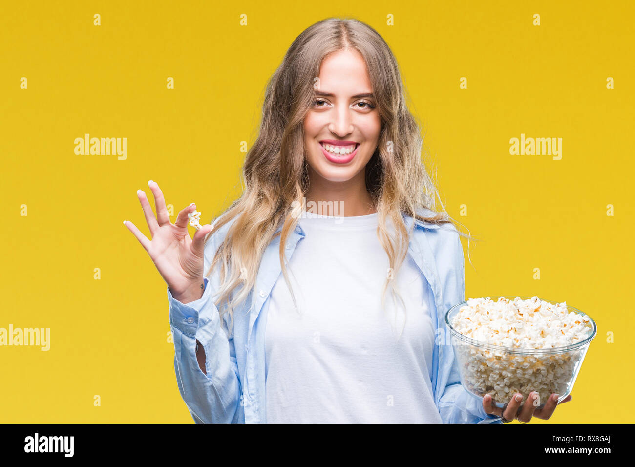 Beautiful young blonde woman eating popcorn over isolated background ...