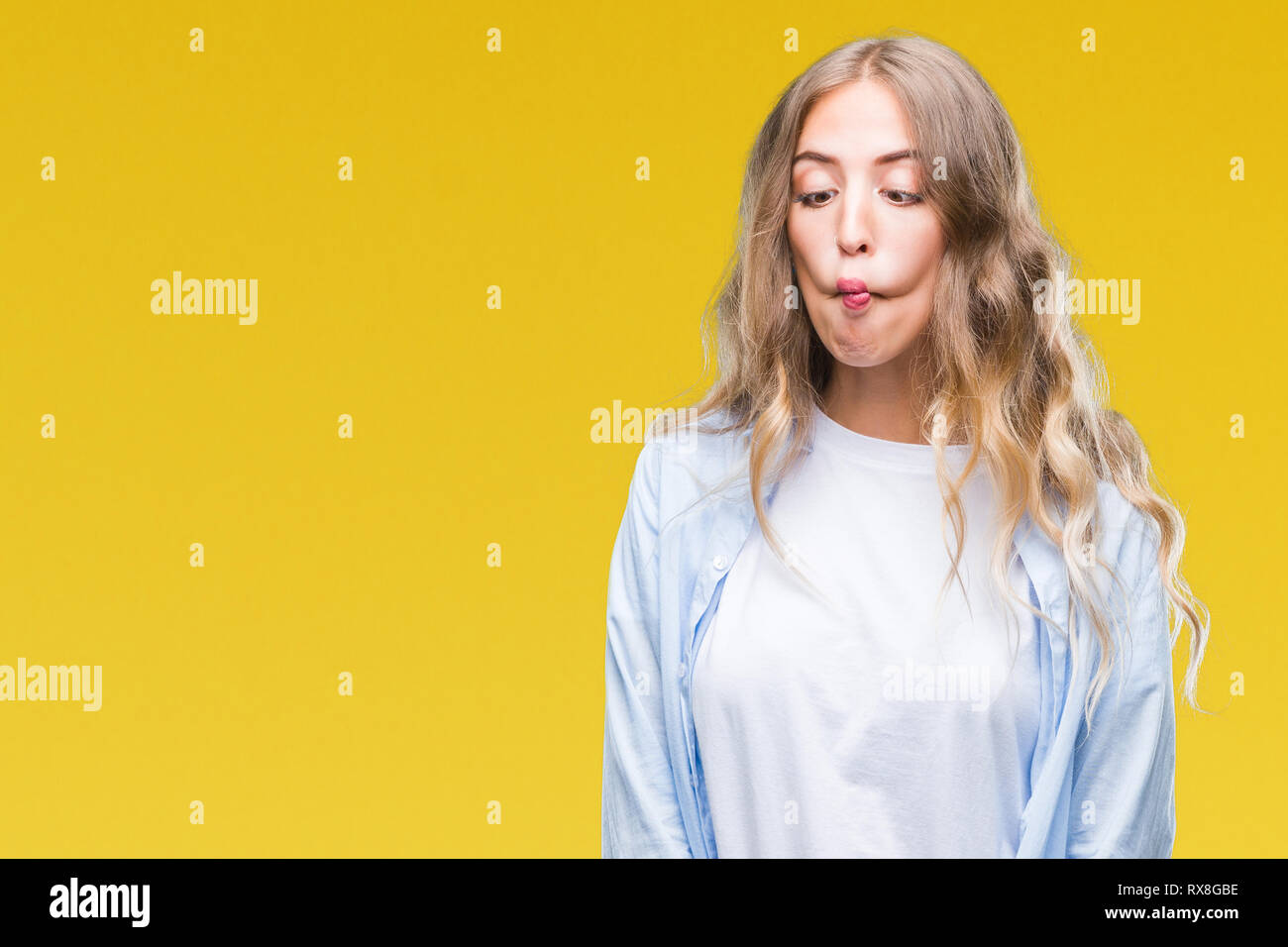 Beautiful young blonde woman over isolated background making fish face ...