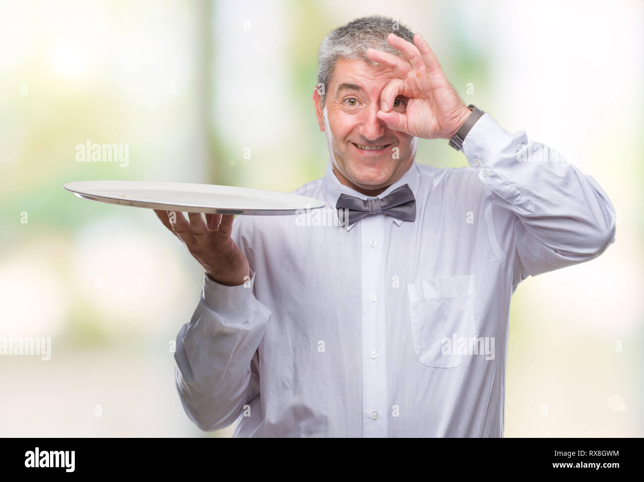 Handsome senior waiter man holding silver tray over isolated background ...