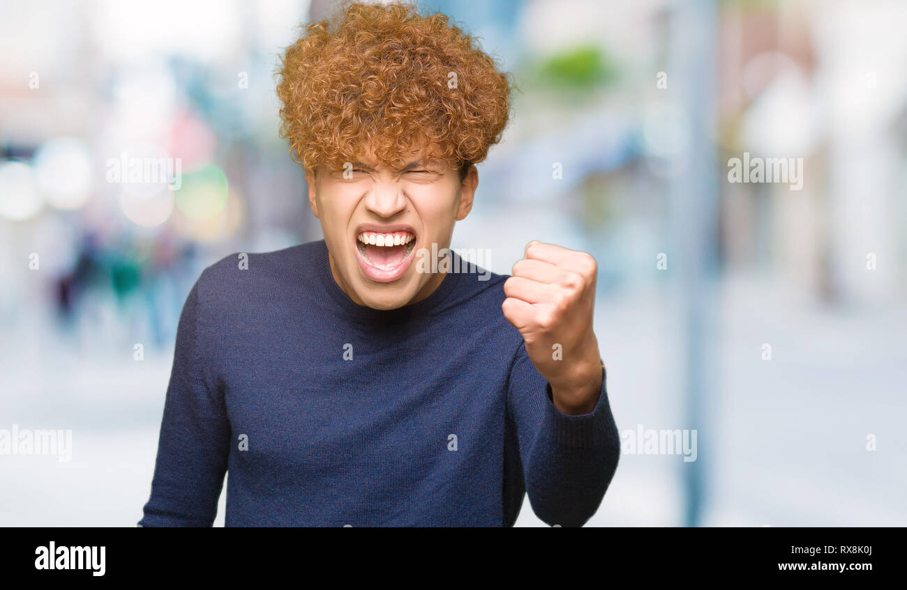 Young handsome man with afro hair angry and mad raising fist frustrated ...