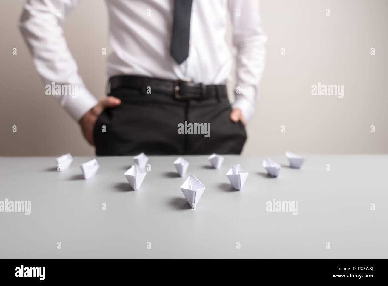 Businessman standing behind a desk with origami paper made boats placed ...