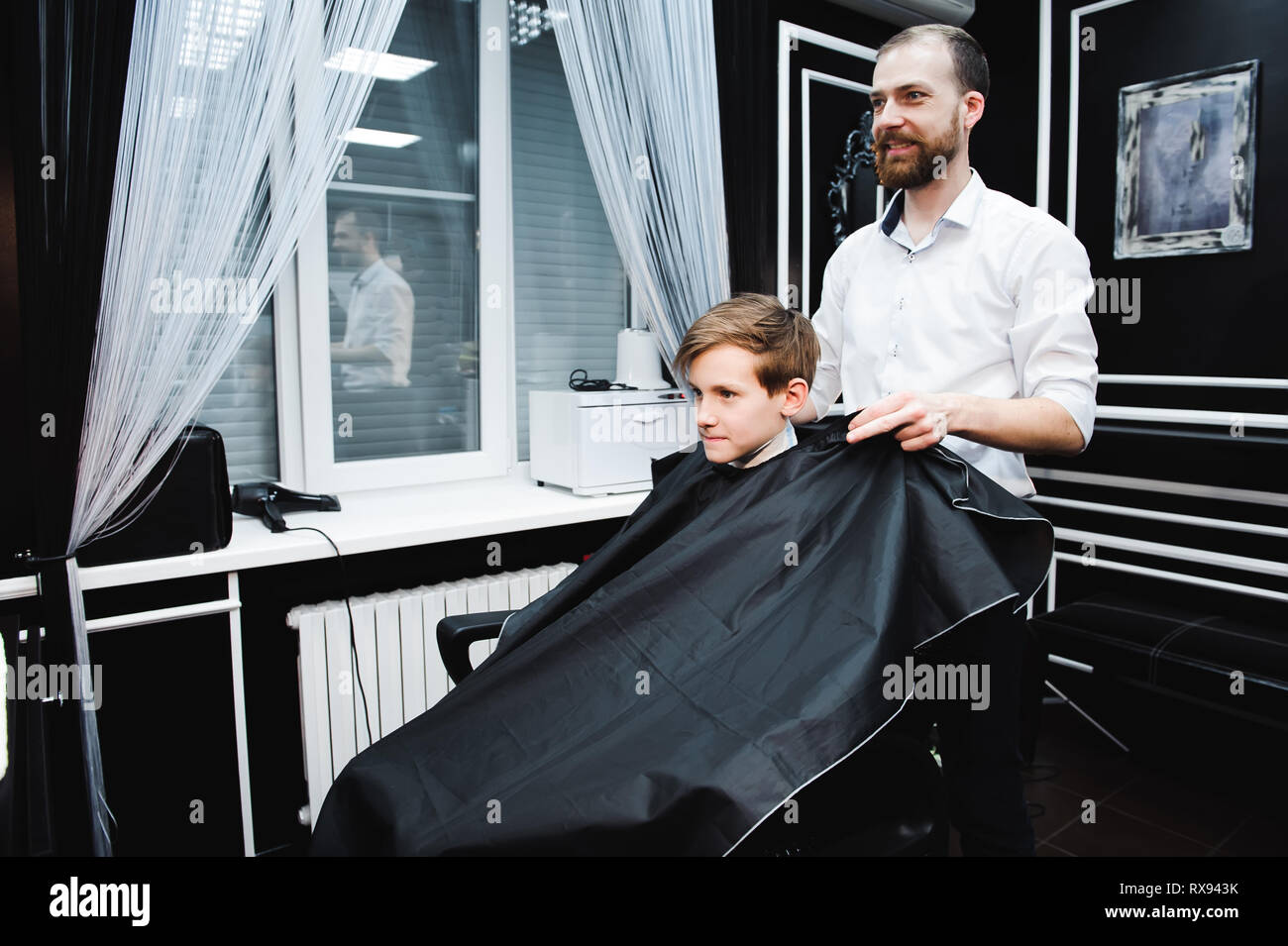 Young handsome barber making haircut of cute boy in barbershop Stock ...