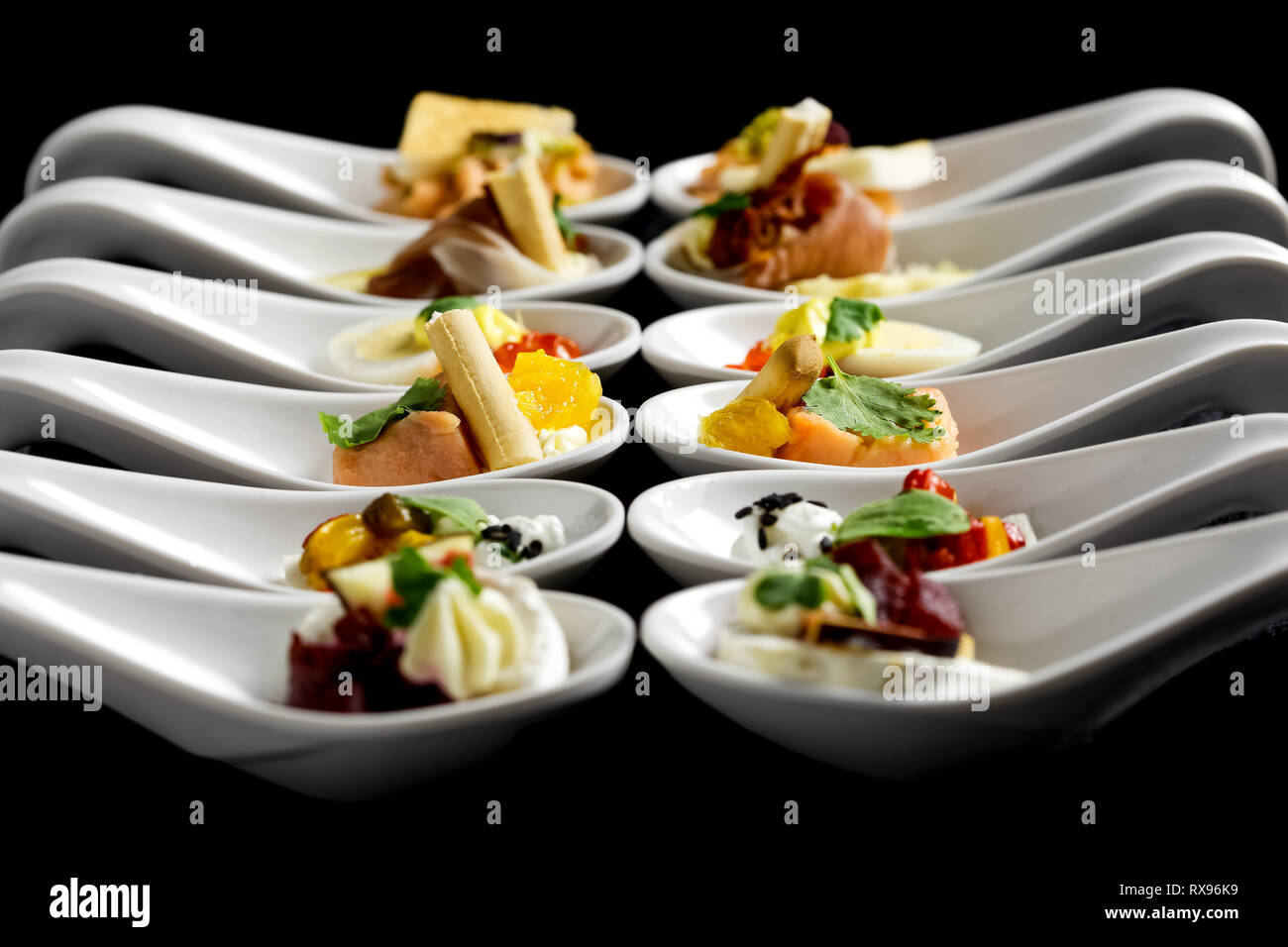Two rows of canapes on white ceramic spoons. Black background Stock ...