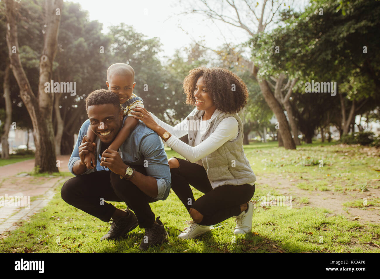 Man carrying his son on his back with woman supporting at park. Happy ...