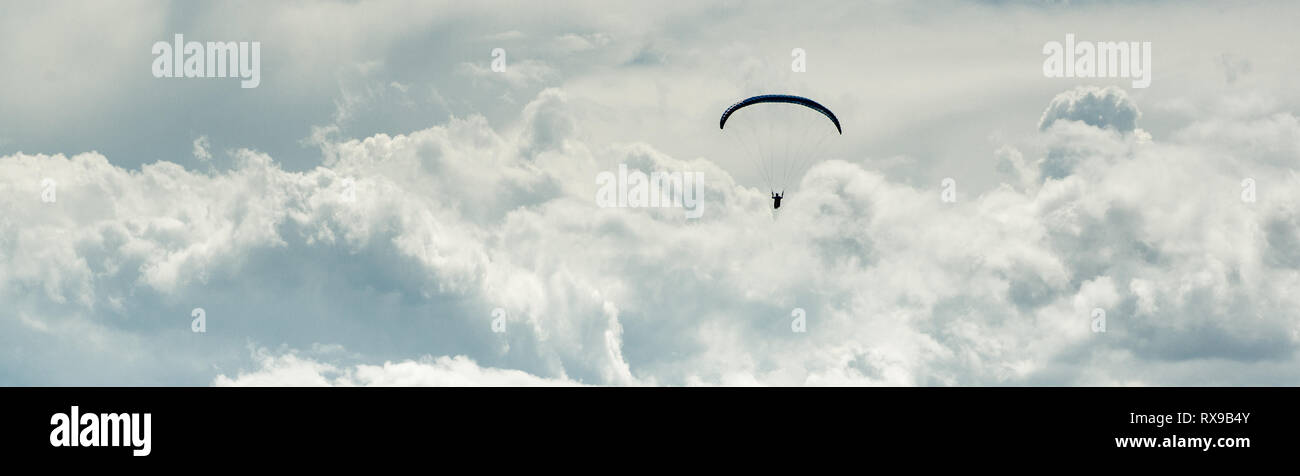 Horizontal cropped image paraglider silhouette over fluffy cloudy sky ...