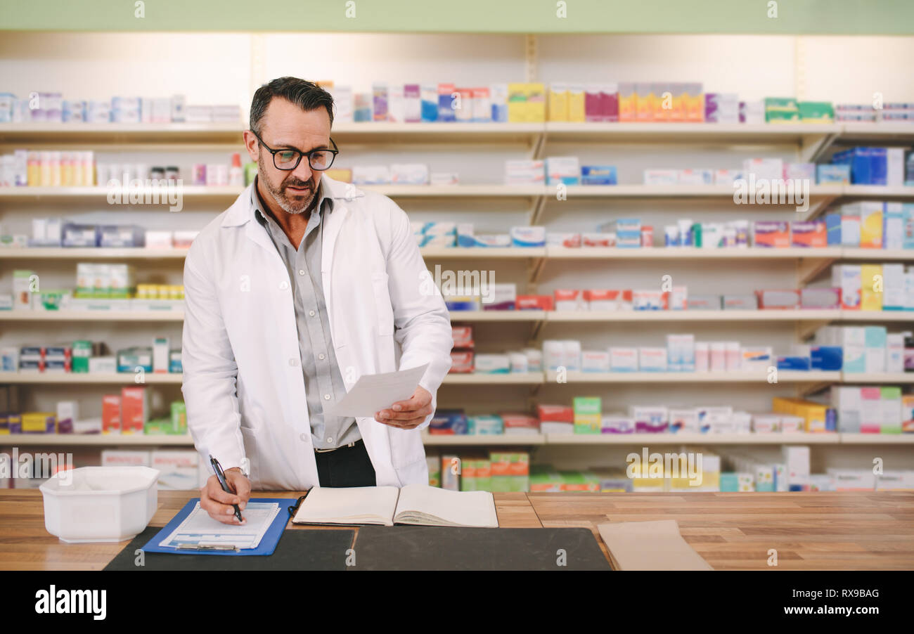 Male pharmacist writing prescription at workplace. Mature male chemist ...