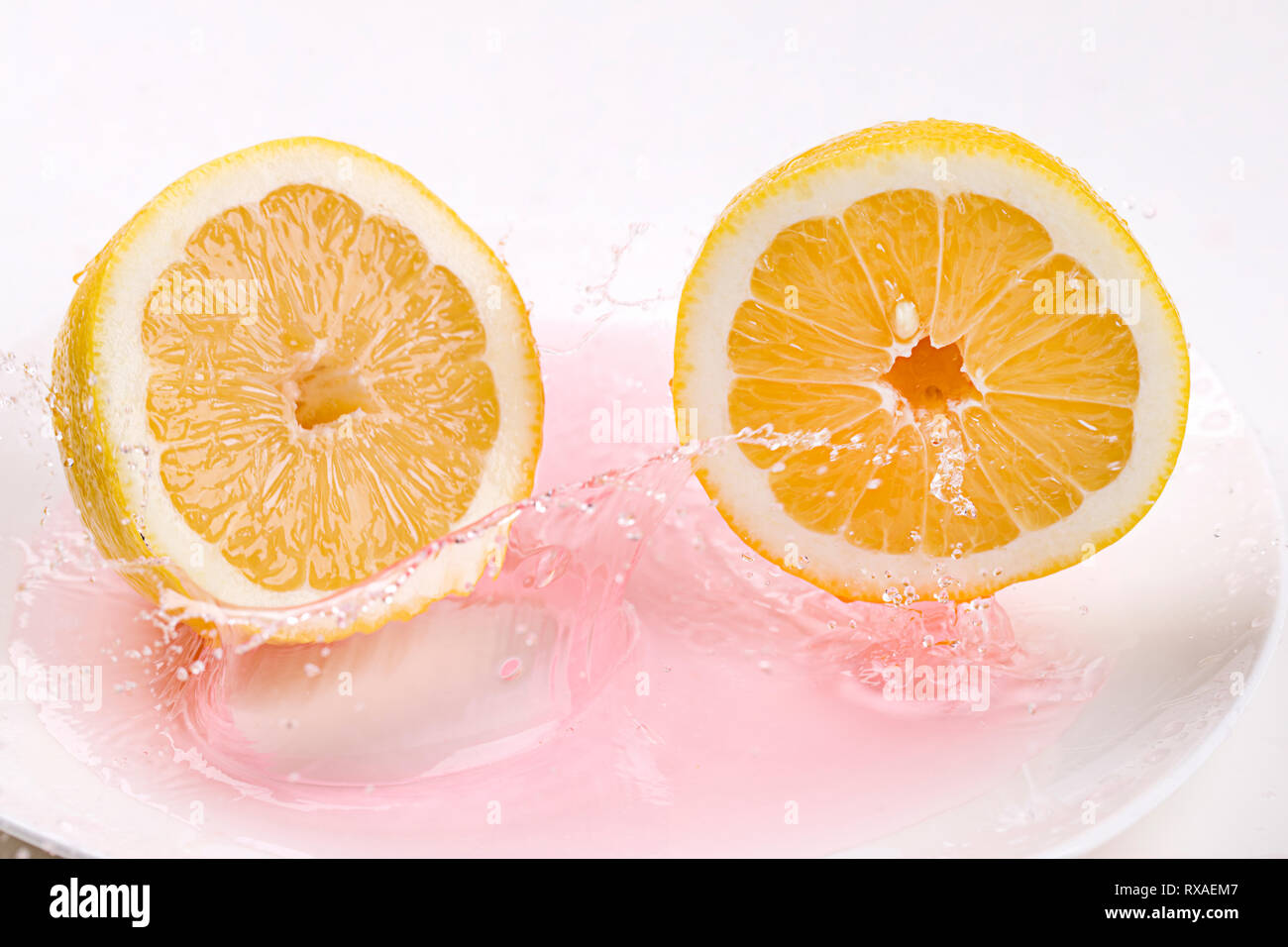 Two lemon halves are dropped into a plate with red tinted water making ...