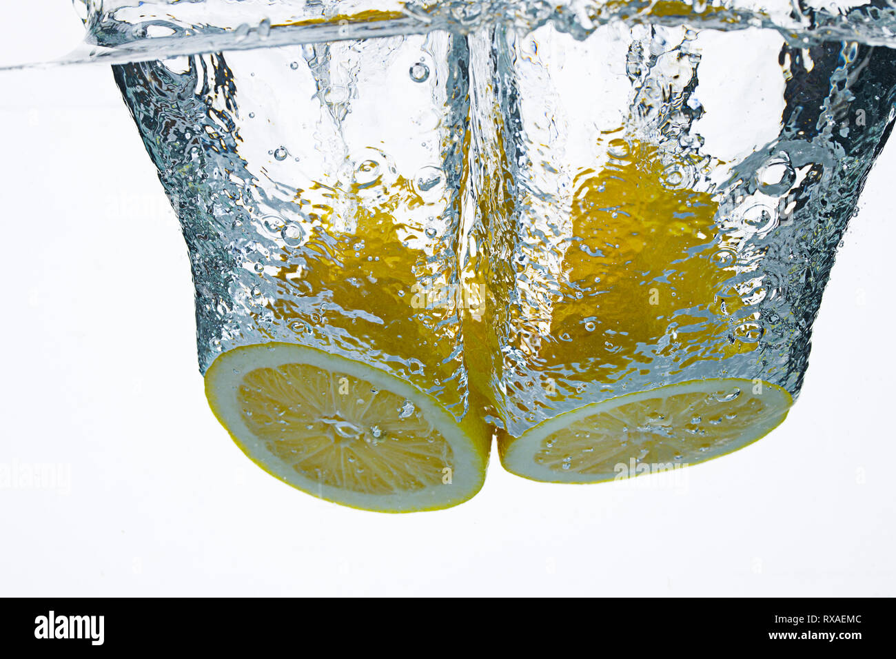 Two lemon halves are dropped into water against a white background ...