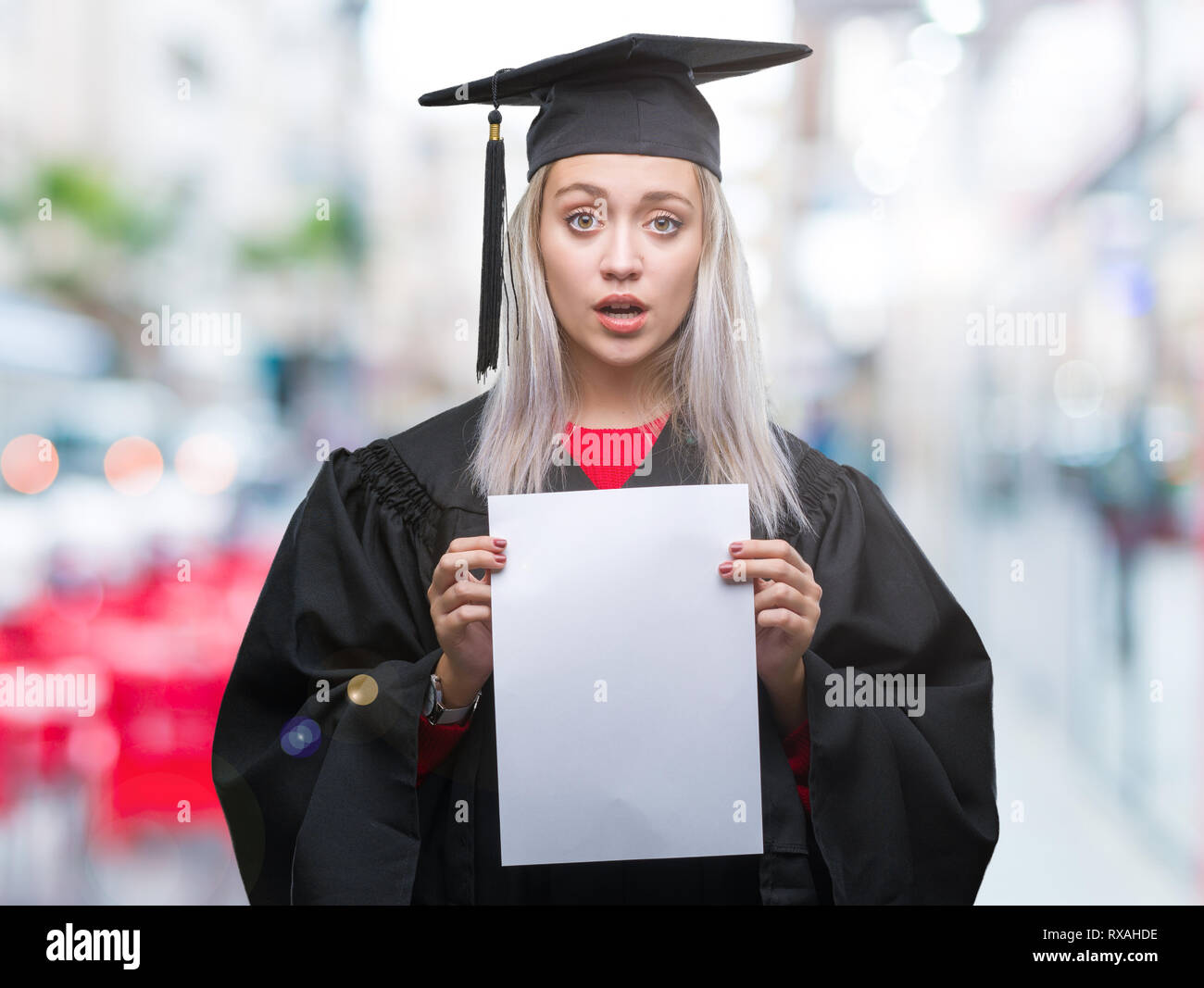 Young blonde woman wearing graduate uniform holding degree over ...