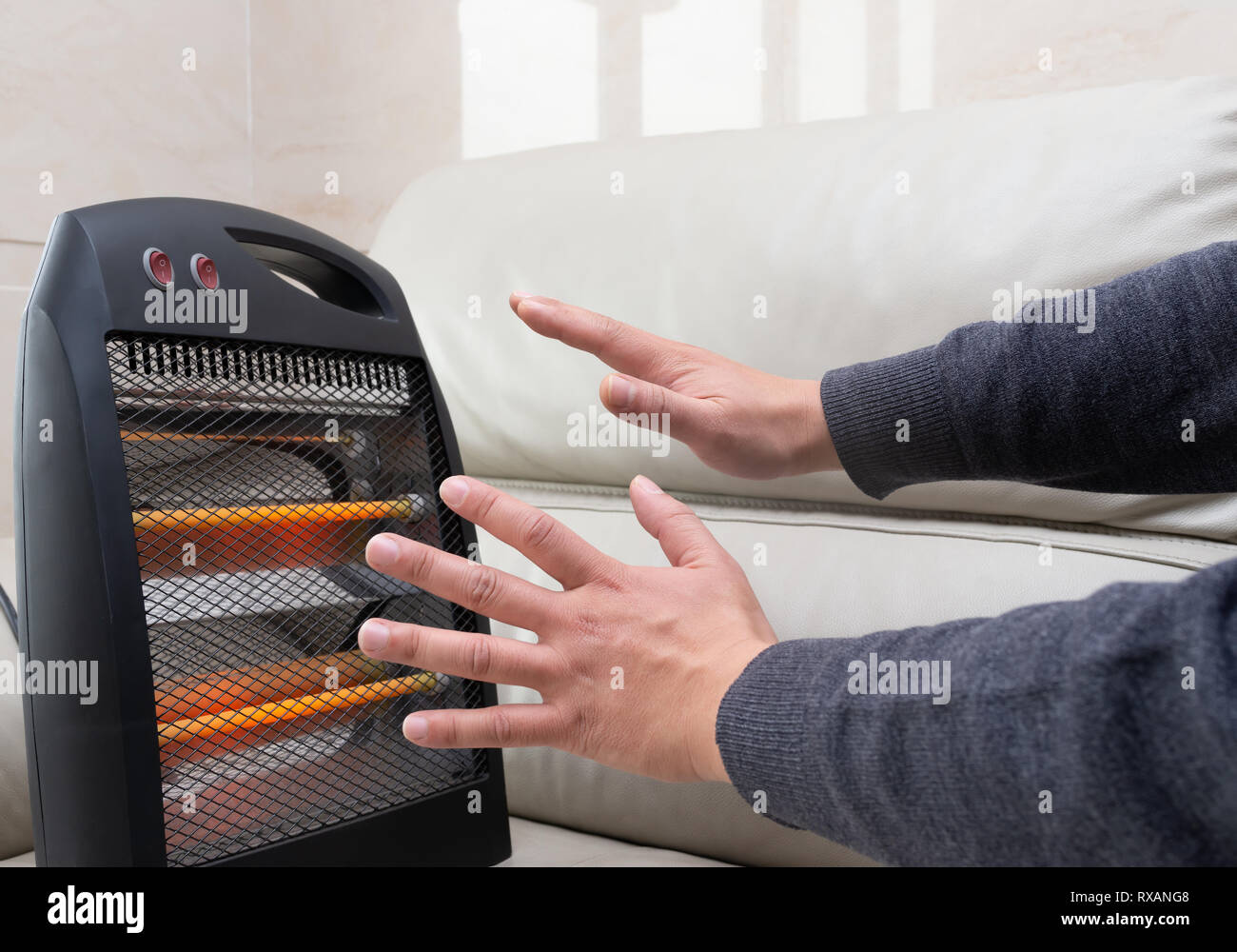 man sitting on sofa and warming up his hands with an electric heater ...