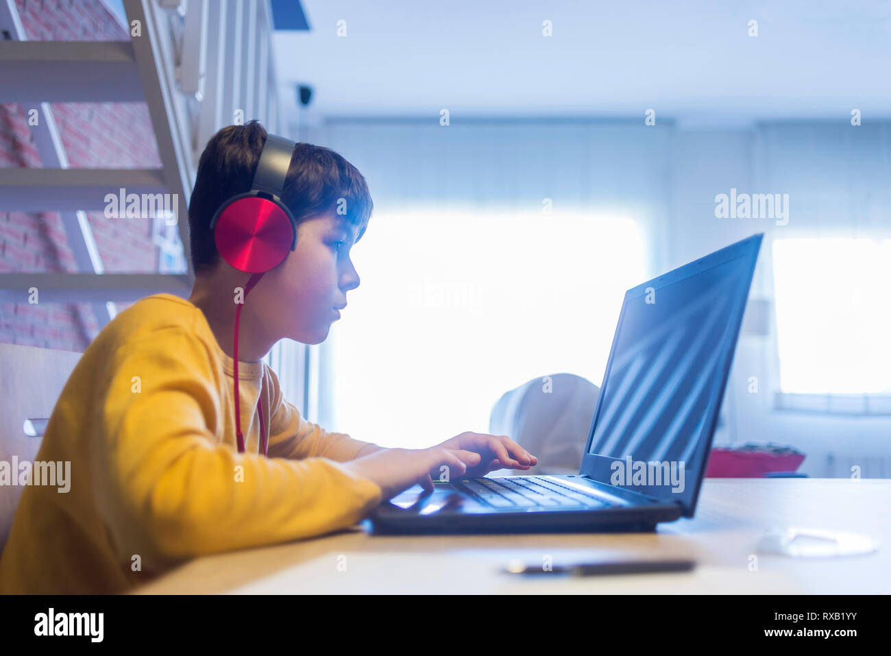 Side view of boy doing homework using headphones and laptop computer at ...