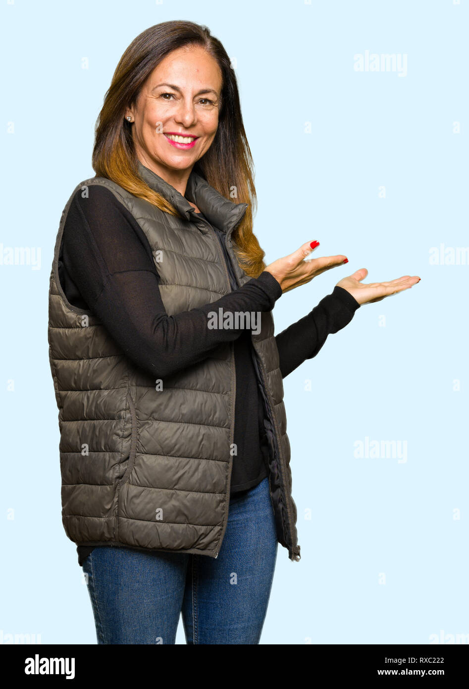 Beautiful middle age woman wearing winter vest Inviting to enter ...