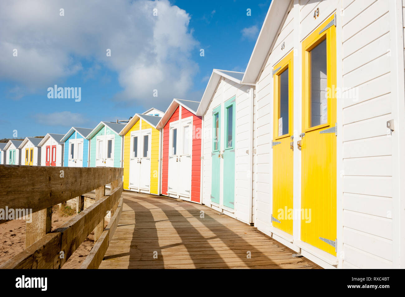 Multi coloured beach huts with wooded boardwalk facing the beach at ...