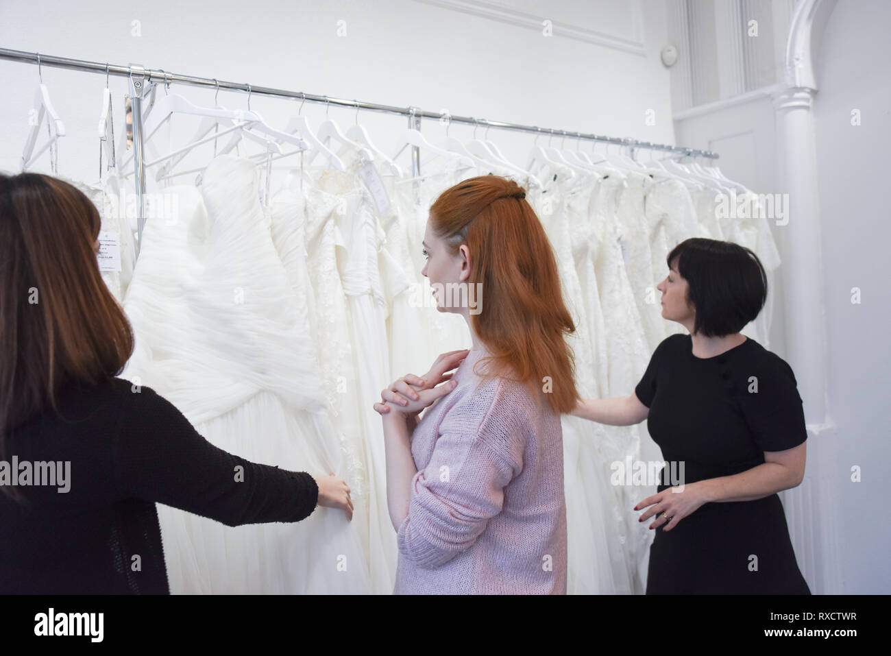 2 shop assistants are helping a pretty red haired girl to choose a ...